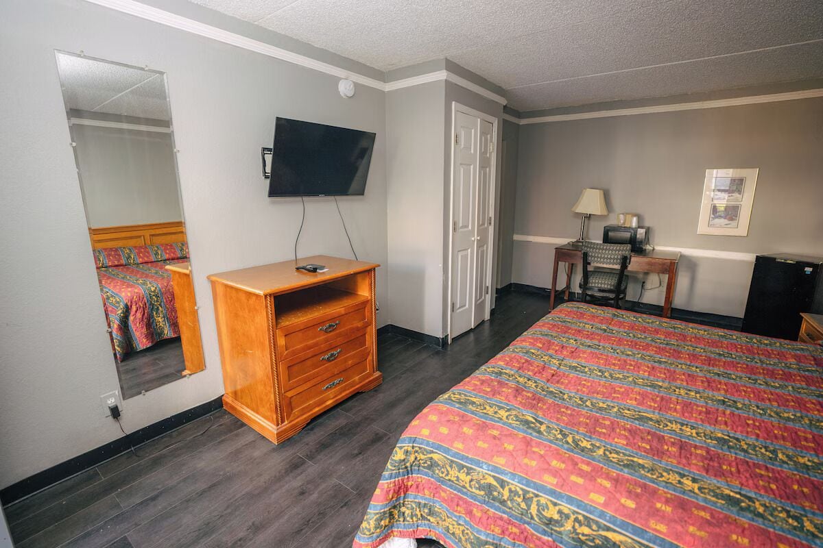 Quarto de hotel com cama, cômoda, televisão, escrivaninha e porta.