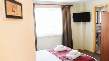 Quarto de hotel com uma cama, uma televisão na parede e uma janela com cortinas.
