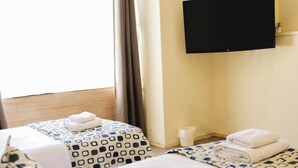 Quarto de hotel com duas camas, uma TV presa na parede e uma janela com cortinas.