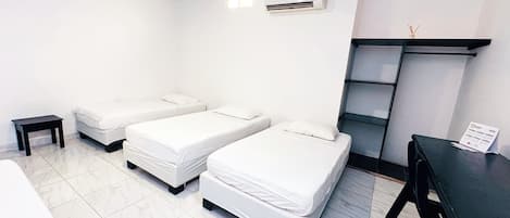 Quarto com duas camas de solteiro, uma mesinha, escrivaninha e estante.