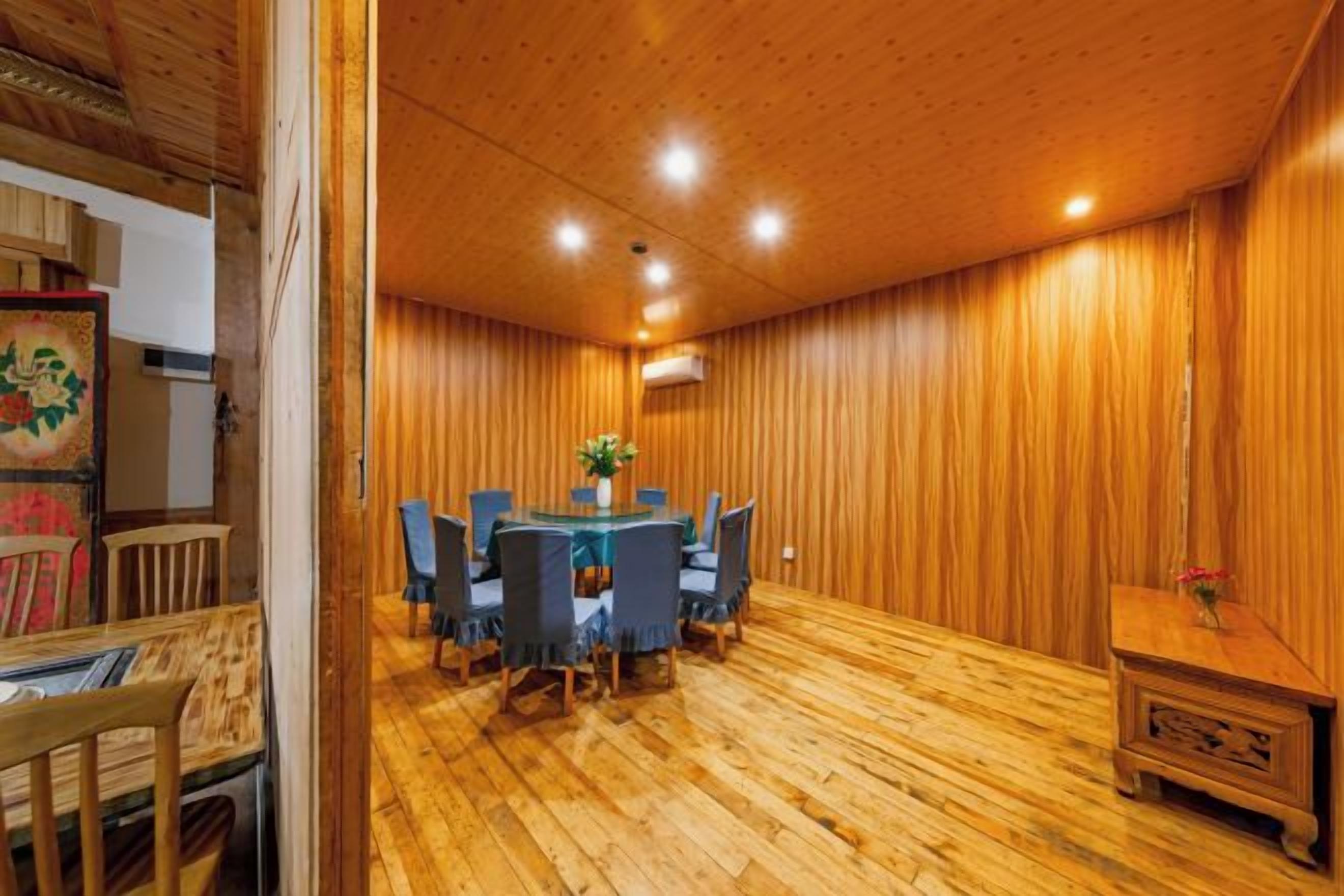 Um quarto com painéis de madeira, uma mesa redonda e cadeiras, um pequeno armário e uma porta que dá para outro aposento.