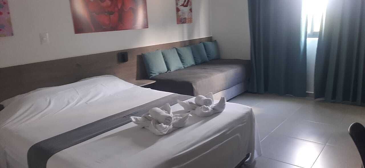 Quarto de hotel com duas camas, um sofá e uma janela com cortinas.