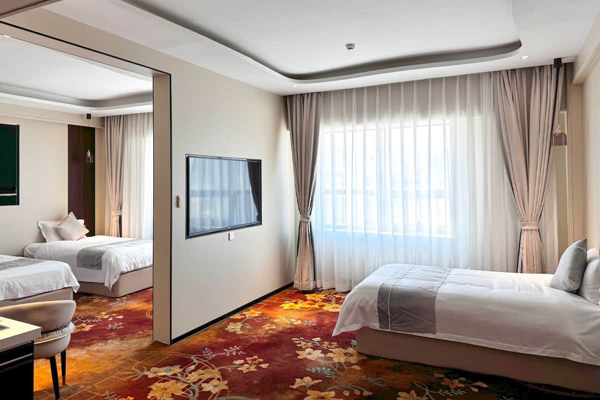 Quarto de hotel com duas camas, um espelho grande, uma televisão de tela plana e uma janela com cortinas leves.