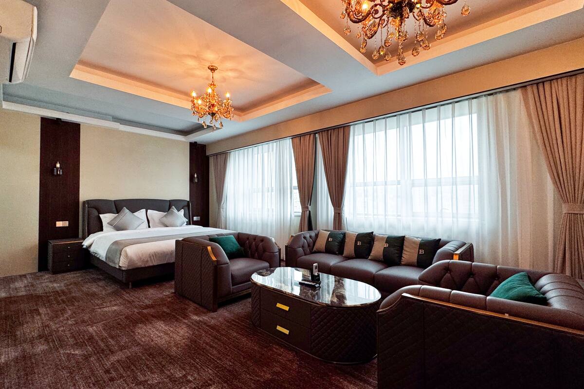 Quarto de hotel espaçoso com uma cama grande, um sofá de couro, uma mesa de centro e um candelabro.