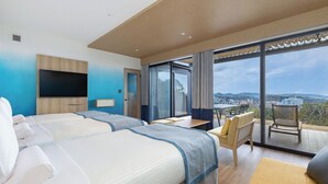 Quarto de hotel moderno com duas camas, TV, varanda com vista e área de jantar.