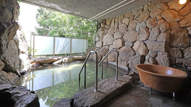 Piscina interior com paredes de pedra, uma banheira de pedra, escadas de metal e uma barreira de vidro.