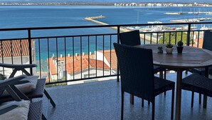 Uma varanda com vista para o mar, uma mesa e cadeiras.