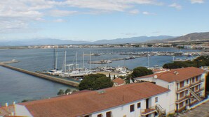 Uma marina costeira com barcos atracados, edifícios com telhados vermelhos e céu claro.