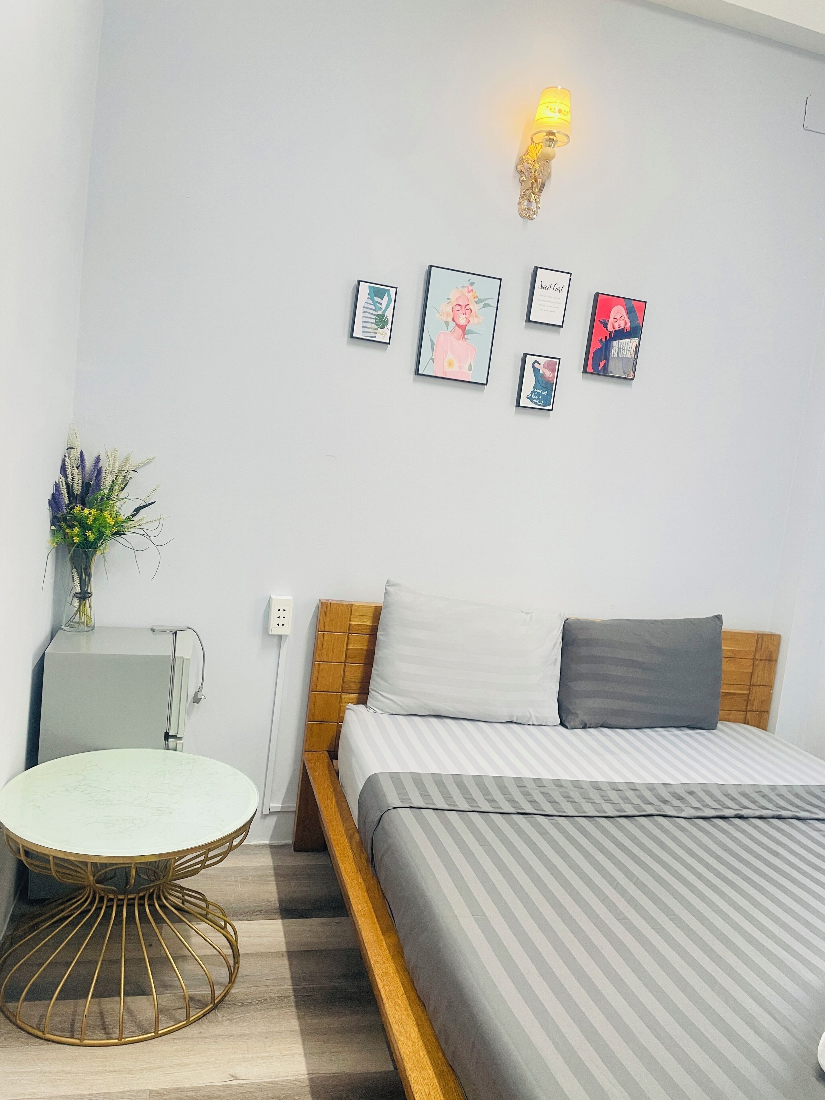 Quarto com cama, mesa de cabeceira, luminária na parede e quadros.