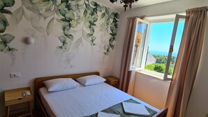 Quarto com cama, mesa de cabeceira, janela com cortinas e parede com padrão de folhas.