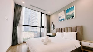 Quarto de hotel moderno com uma cama grande, mesa de cabeceira, espelho e vista para edifícios altos pelas amplas janelas.