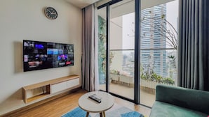 Uma sala de estar moderna com uma televisão de tela plana, um sofá, uma mesa redonda pequena e uma varanda com vista para um horizonte urbano.