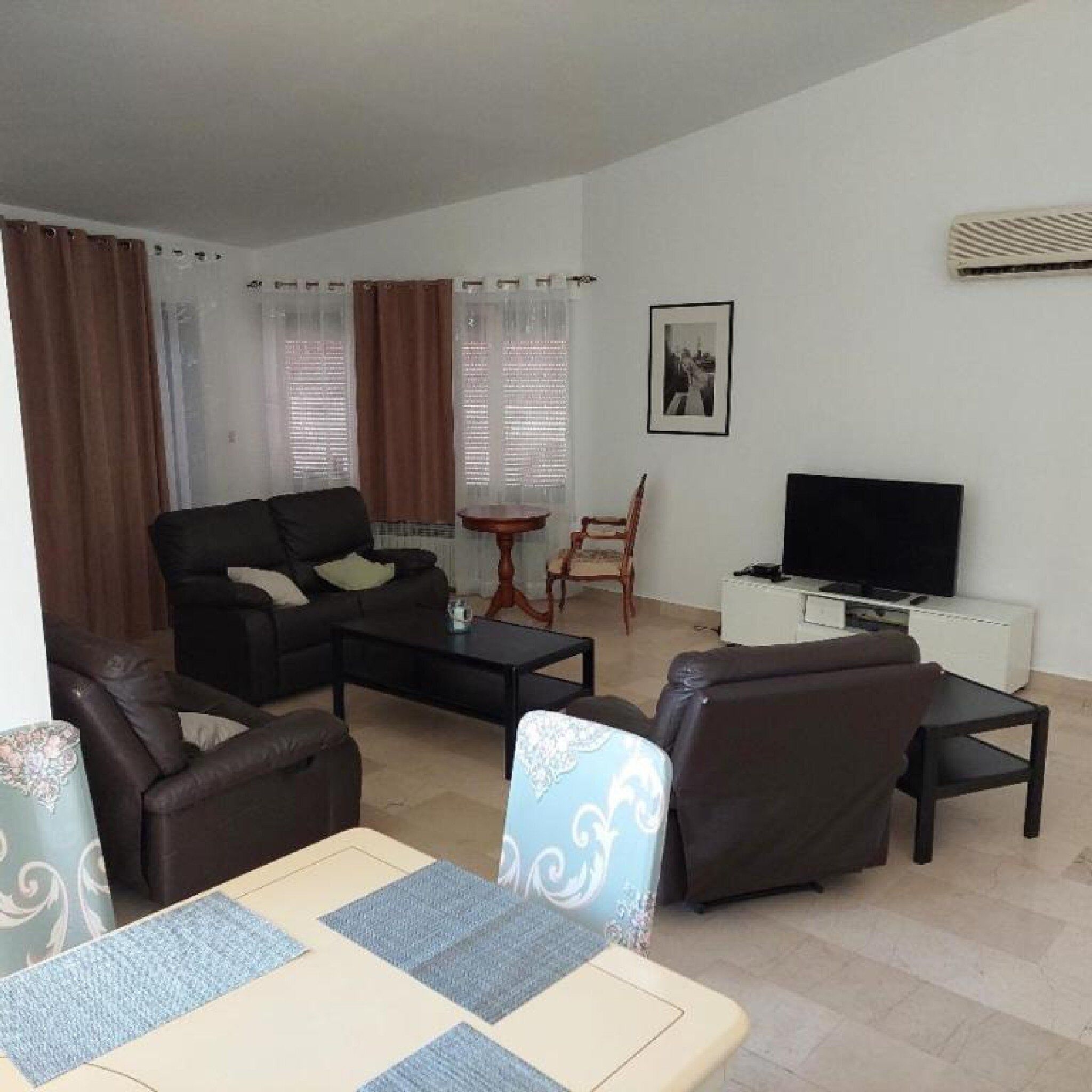 Uma sala de estar com sofá, poltronas, mesa de centro, televisão e uma mesinha com porta-retrato.
