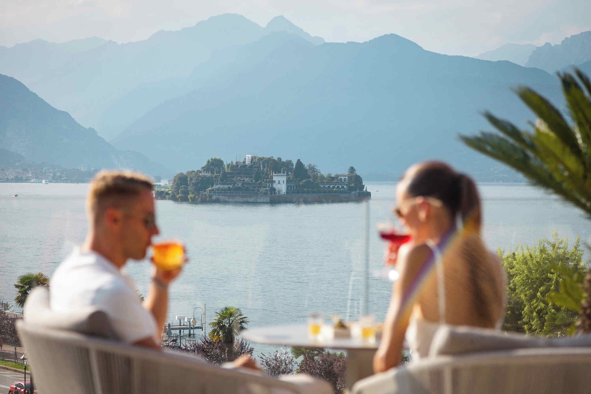 Um casal jantando à mesa com vista para um lago e montanhas.