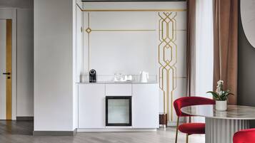 Quarto de hotel moderno com design minimalista, com uma pequena cozinha, área de jantar com cadeiras vermelhas e uma grande janela com cortinas.