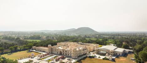 Um grande edifício histórico com várias cúpulas e pátios, rodeado por vegetação exuberante e colinas ao longe.