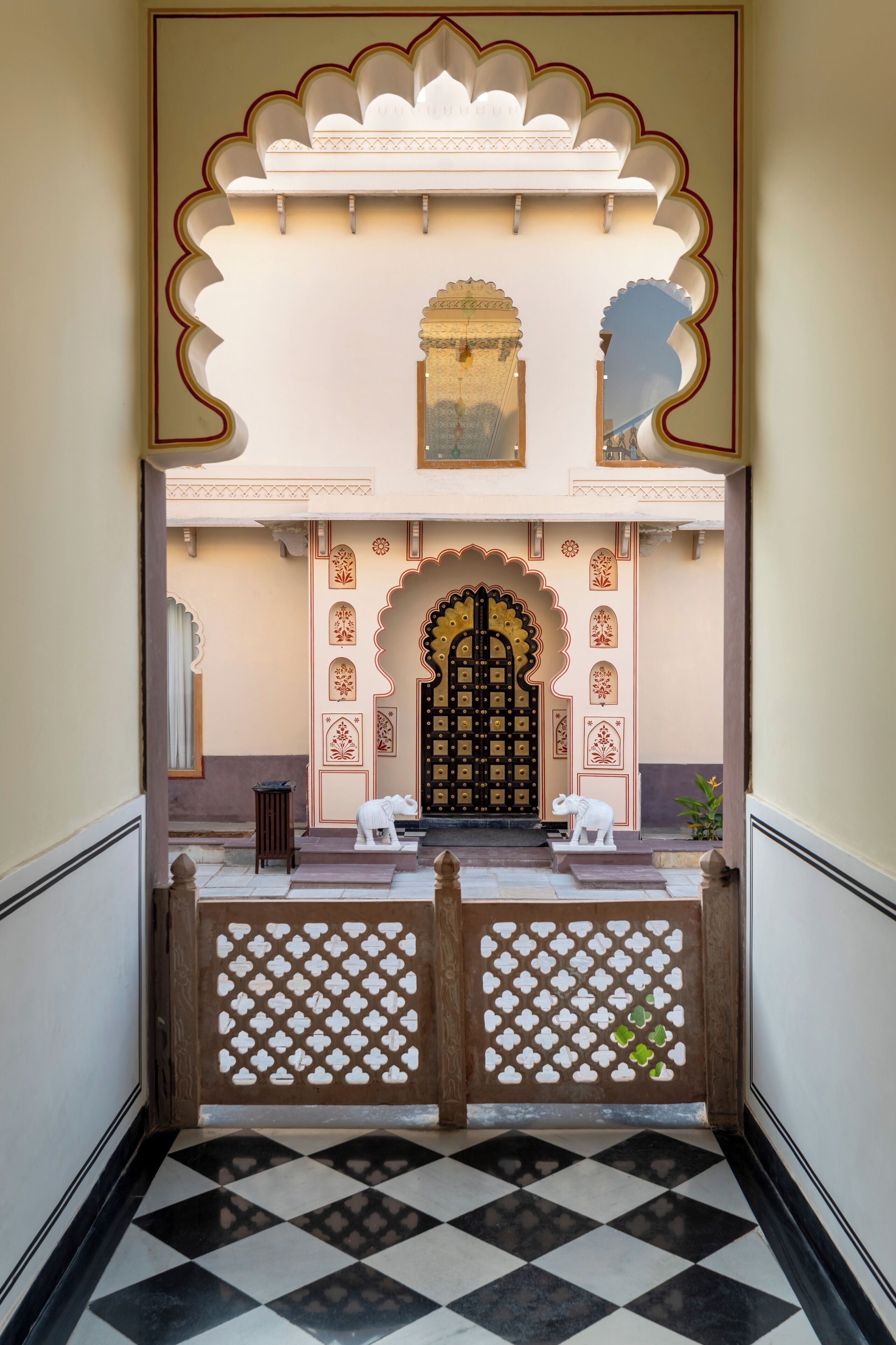 Um corredor com piso xadrez, um arco decorativo e uma porta preta com detalhes elaborados.