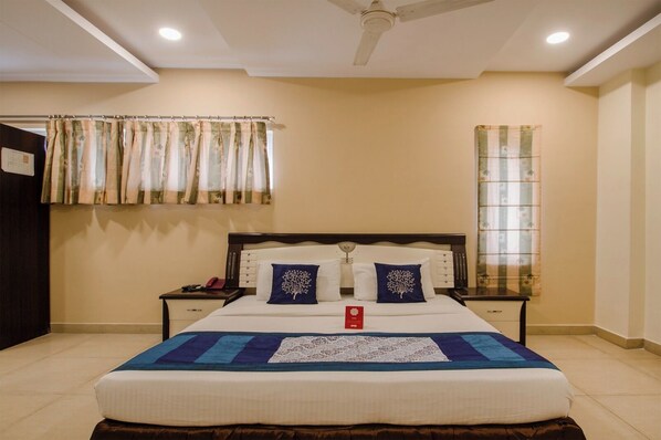 Quarto de hotel bem arrumado, com uma cama, mesa de cabeceira, telefone e janela com cortinas.