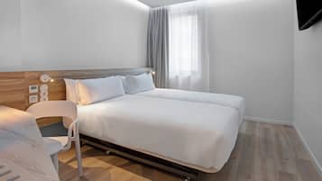 Quarto de hotel moderno com cabeceira de madeira, uma cama de solteiro, uma cadeira branca e uma televisão de tela plana fixada na parede.