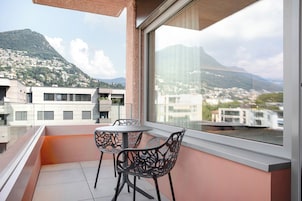 Varanda com mesa e cadeiras, vista para um horizonte urbano com edifícios e uma montanha.