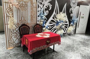 Um quarto com toalha de mesa vermelha, duas cadeiras, parede decorativa e um arranjo floral.