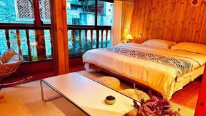 Um quarto aconchegante com teto de madeira, cama com roupa de cama estampada, mesa de cabeceira com abajur e vista para o exterior pela janela.