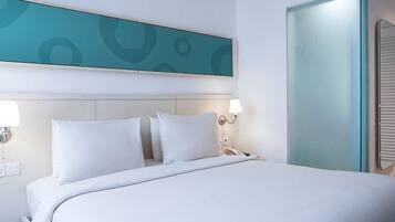 Quarto de hotel com cama, duas luminárias de cabeceira, telefone e espelho.