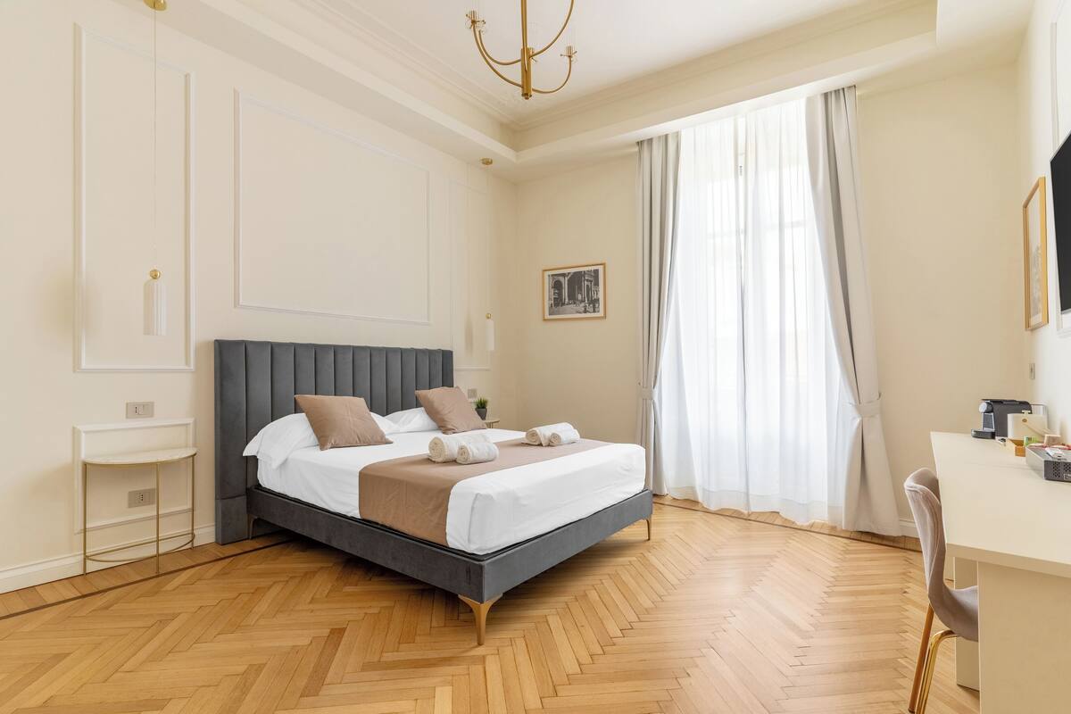 Quarto de hotel moderno com uma cama grande, uma mesa de escritório e vista para a cidade pela janela.