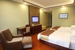 Quarto de hotel com cama, escrivaninha, cadeira, televisão e um quadro na parede.
