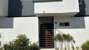 Um edifício moderno de dois andares com telhado plano, entrada central com porta de vidro e uma pequena janela acima da porta.