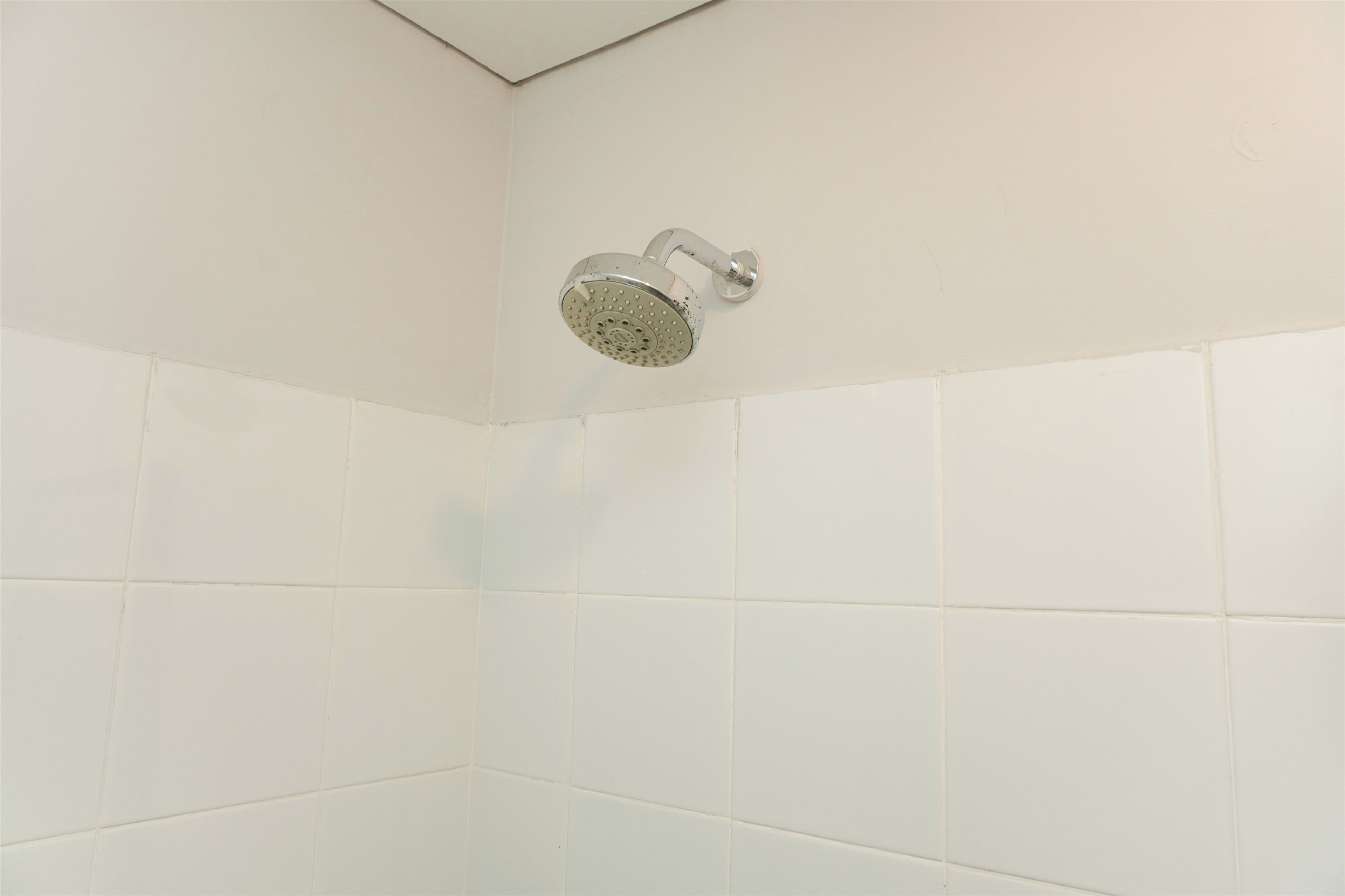 Um canto de casa de banho com paredes revestidas a azulejos brancos e um chuveiro fixo na parede.