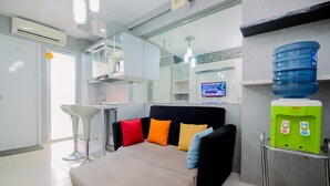 Quarto de hotel moderno com uma cama, televisão, dispensador de água e cozinha compacta.