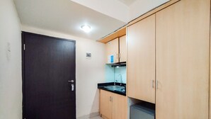 Uma cozinha compacta com porta escura, armários de madeira, bancada preta e um refrigerador pequeno.