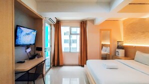 Quarto de hotel com uma cama, escrivaninha com computador, televisão e janela com cortinas.