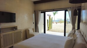 Quarto de hotel com uma cama grande, TV presa na parede e vista para uma paisagem desértica com cactos.