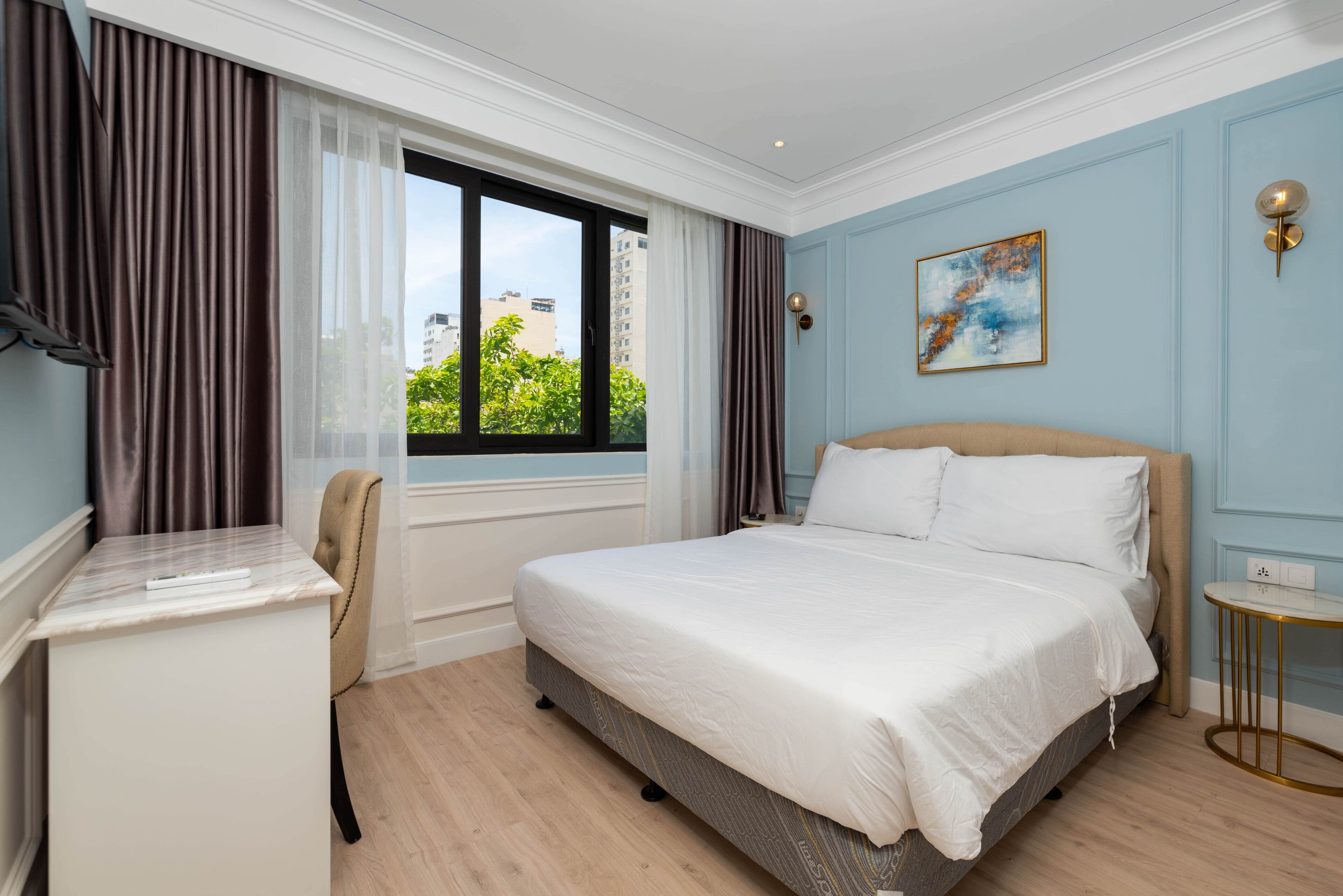 Quarto de hotel com cama, escrivaninha, cadeira, janela com cortinas e um quadro na parede.