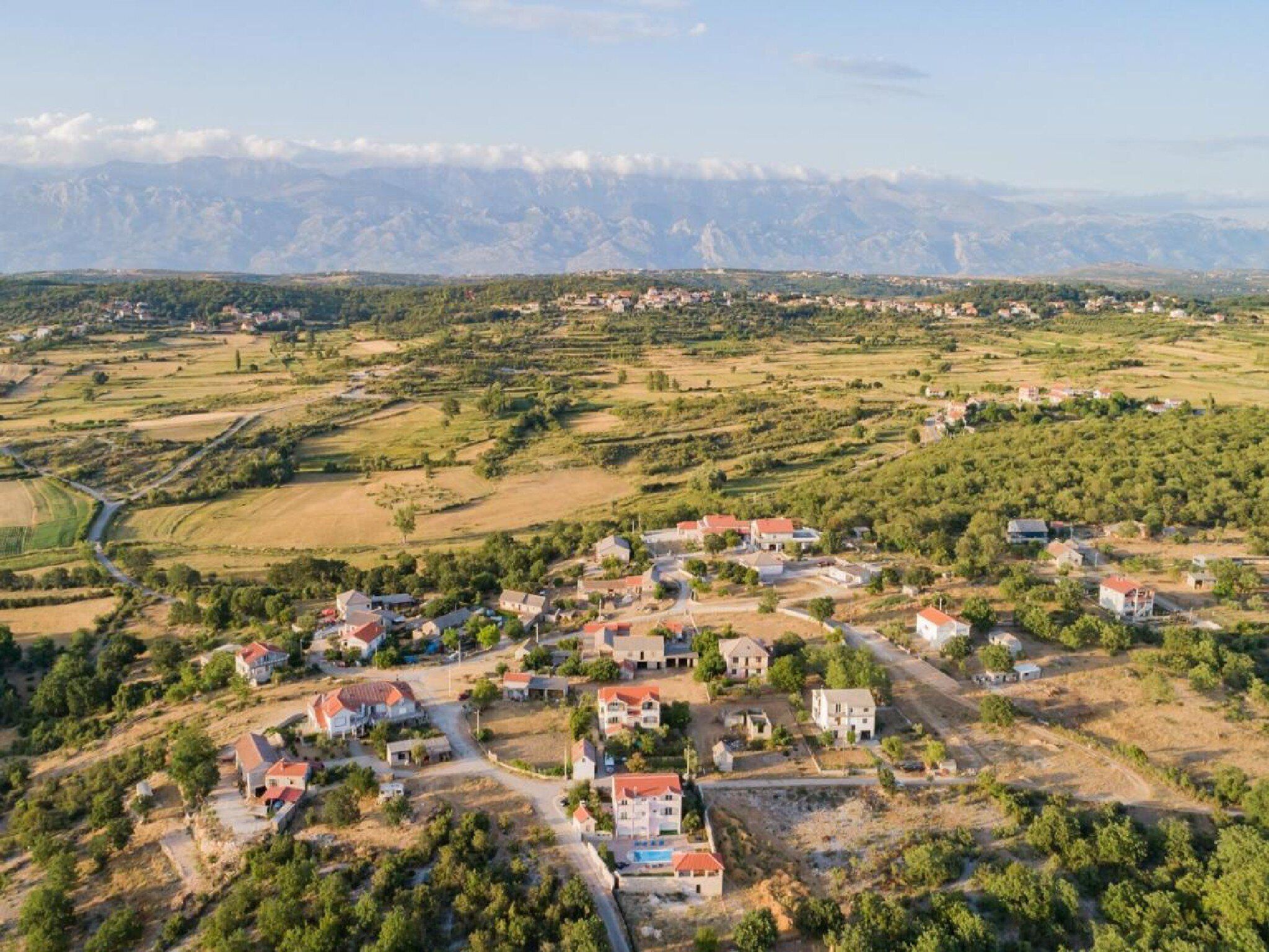 Uma vila rural com casas e campos, rodeada por montanhas.