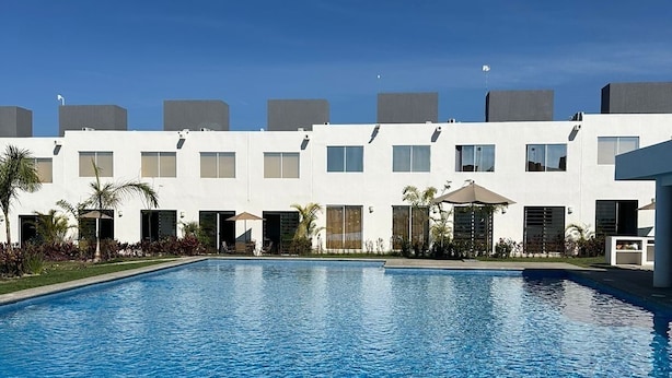 Piscina com superfície de água azul e límpida, rodeada por um edifício branco com várias janelas e varandas.