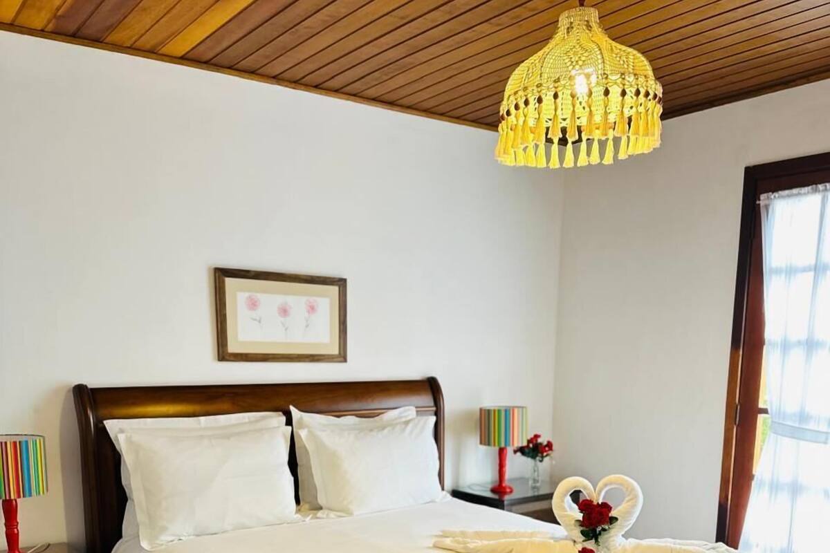 Uma cama bem arrumada com um cobertor listrado em rosa e branco, uma cabeceira de madeira e um lustre amarelo pendurado.