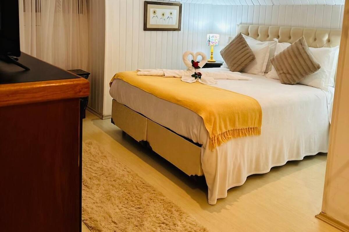 Quarto com cama, mesa de cabeceira, abajur e quadro na parede.
