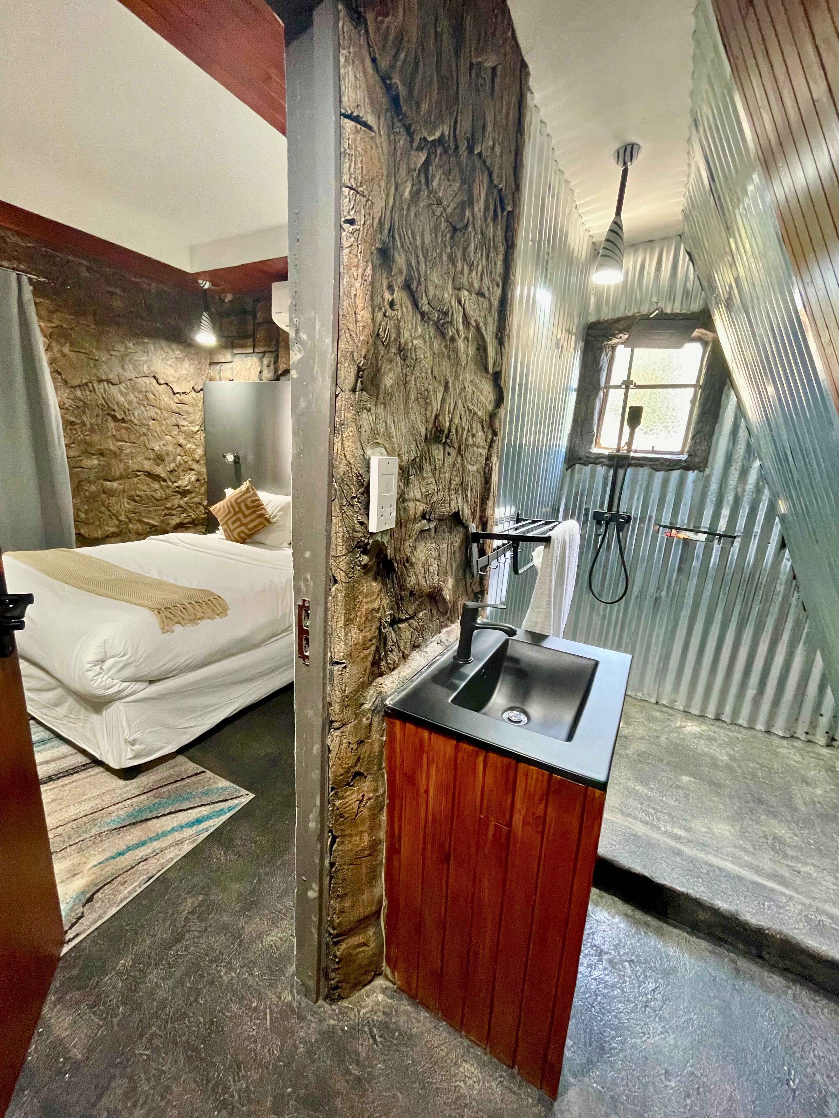Quarto com cama, toucador de madeira com pia, parede de pedra e janela.
