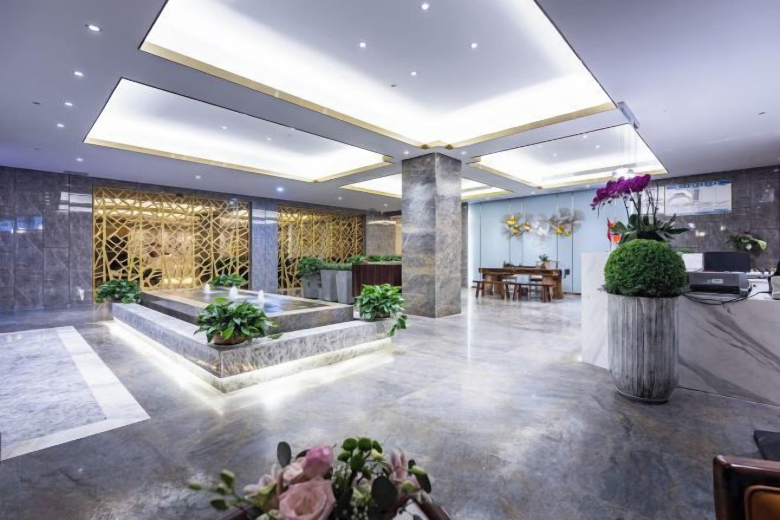 Um hall de hotel moderno, com balcão de recepção, área de estar e plantas decorativas.