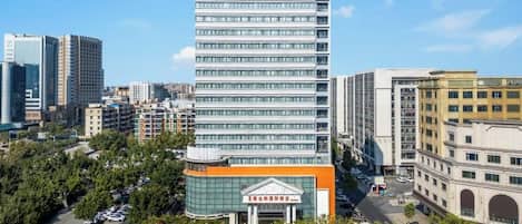 Um hotel de vários andares com entrada destacada, rodeado por outros edifícios e árvores.