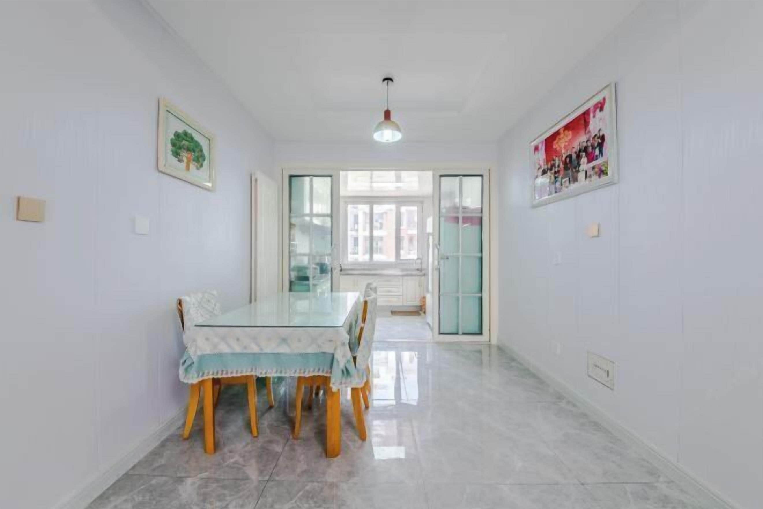 Uma sala de jantar com mesa de vidro, cadeiras de madeira e piso em tons claros.
