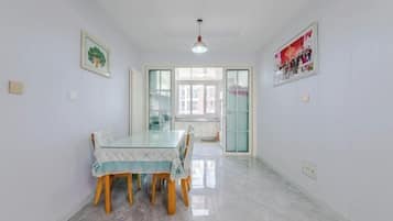 Uma sala de jantar com mesa de vidro, cadeiras de madeira e piso em tons claros.