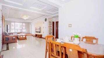 Uma sala de estar ampla com área de jantar, sofás, televisão e decoração na parede.