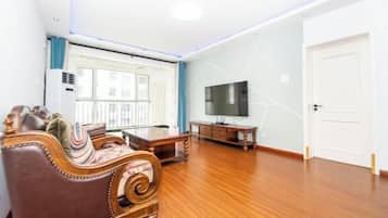 Uma sala de estar com sofá, televisão, piso de madeira e uma porta.