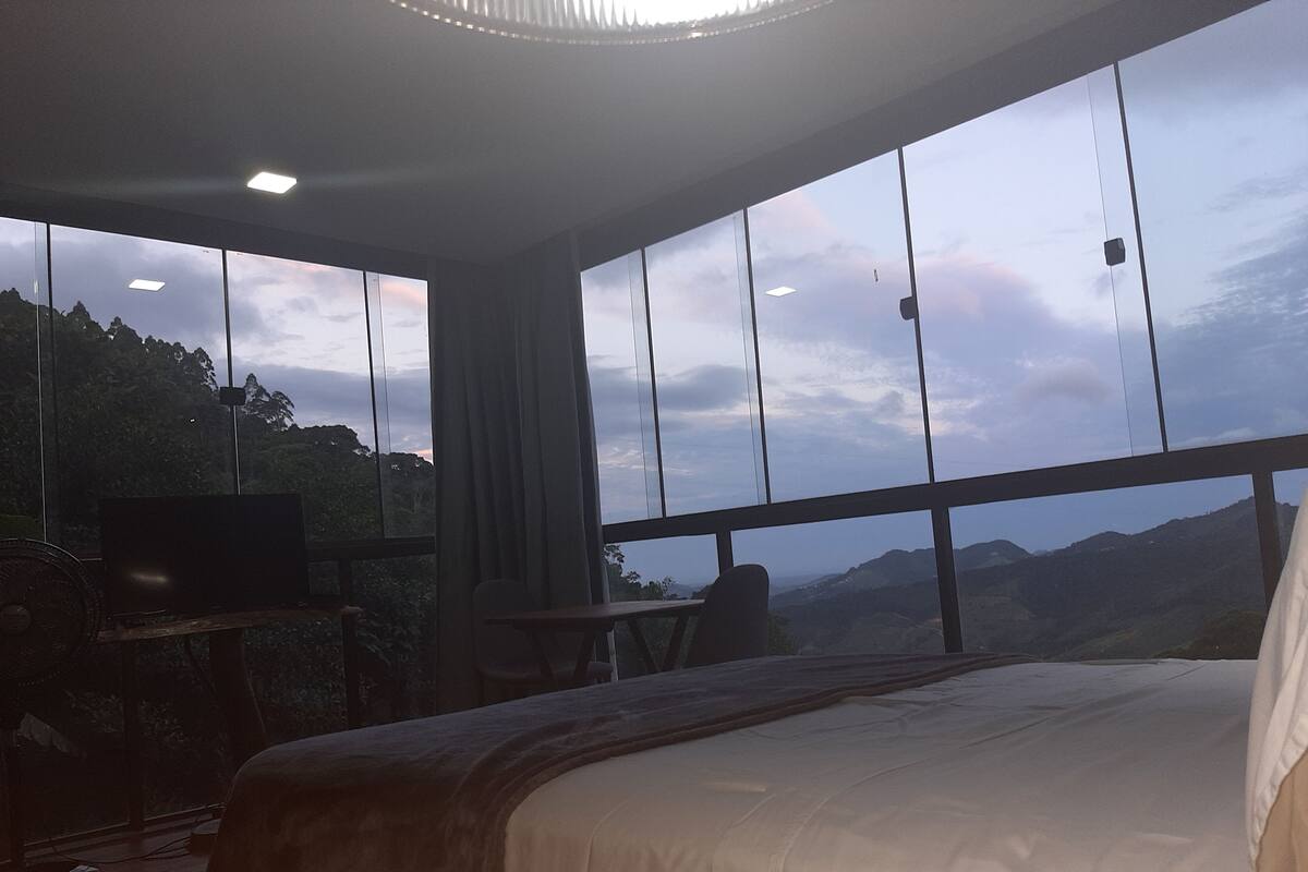 Quarto com uma grande janela que oferece vista para uma paisagem montanhosa.