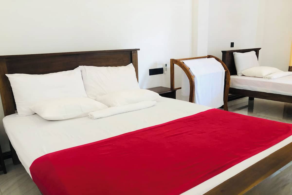 Quarto de hotel com uma cama grande, cabeceira de madeira, manta vermelha e mesa de cabeceira pequena.