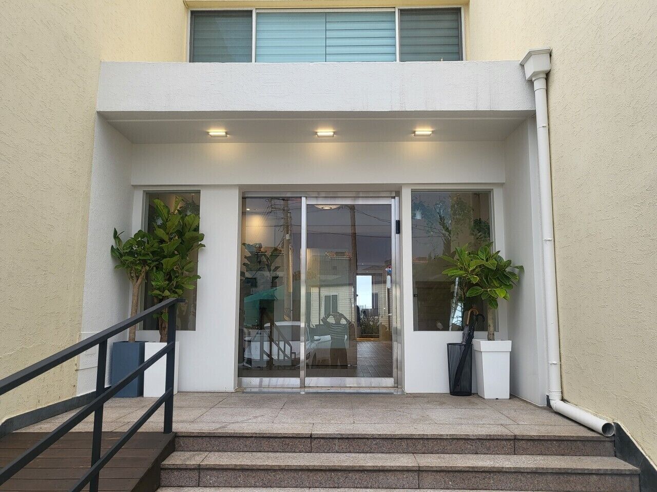 Entrada de um edifício com porta de vidro, escadas e plantas em vasos.